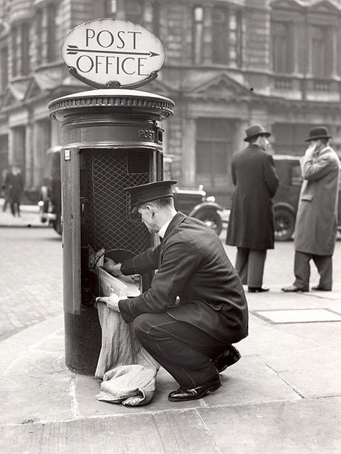 Original postbox with a smarty dressed Royal Mail worker emptying the ...